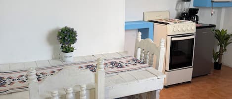 Uma área de refeições com mesa e cadeiras, uma cozinha com eletrodomésticos e uma parede com um quadro emoldurado.