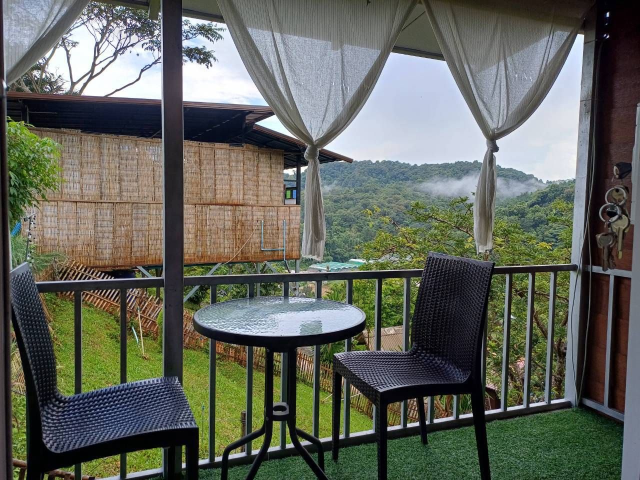 Uma área de estar coberta ao ar livre com duas cadeiras e uma mesa, com vista para uma paisagem exuberante.