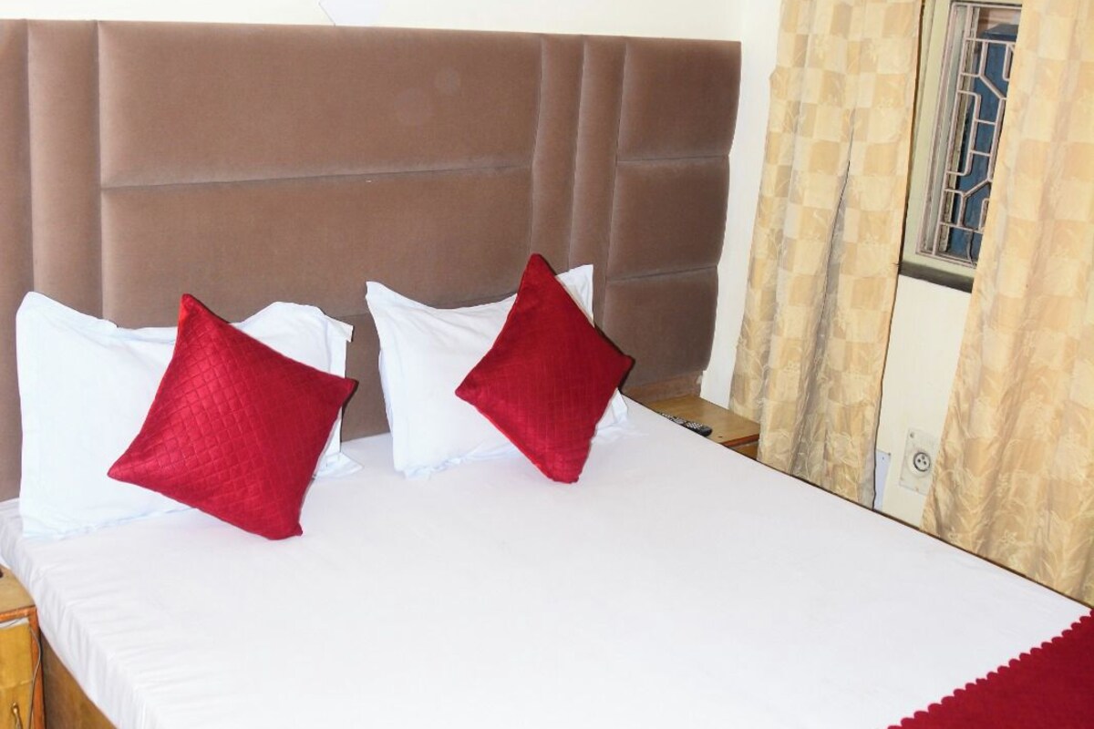 Cama com cabeceira, roupa de cama branca e duas almofadas vermelhas.