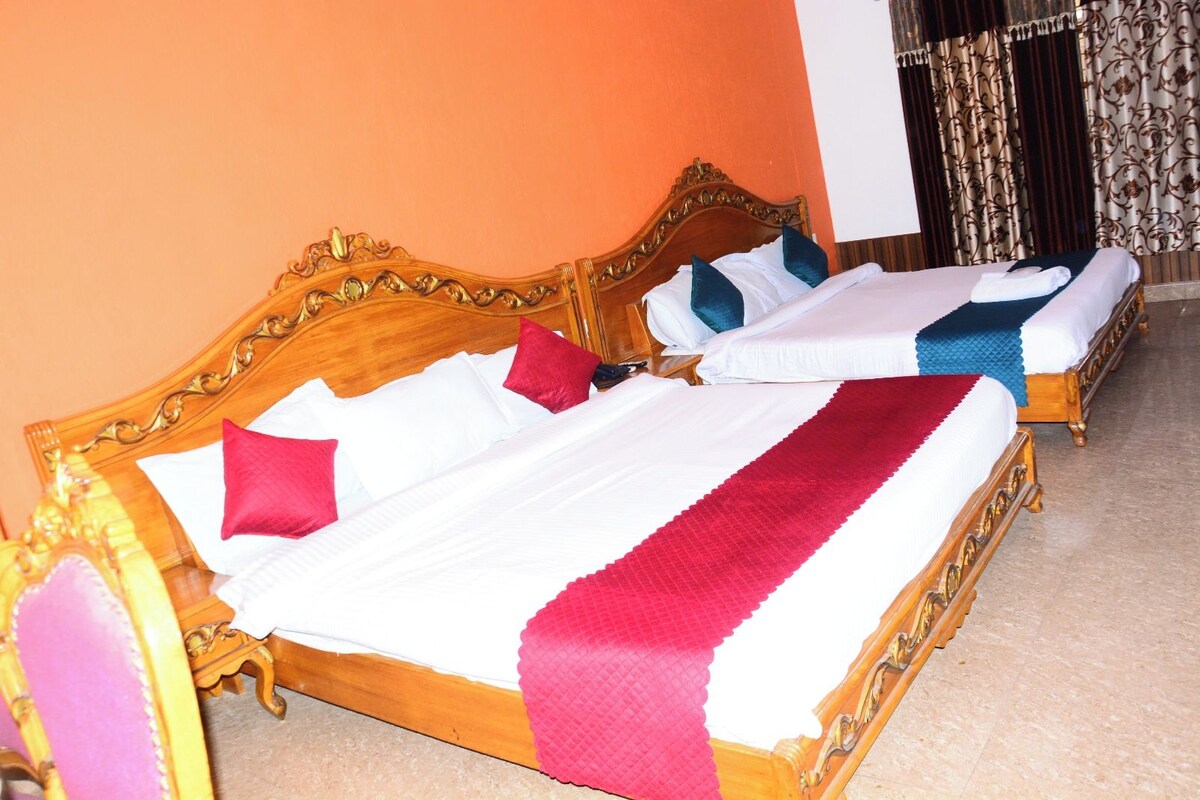 Quarto de hotel com duas camas de casal, uma com colcha vermelha e branca e outra com colcha azul e branca.
