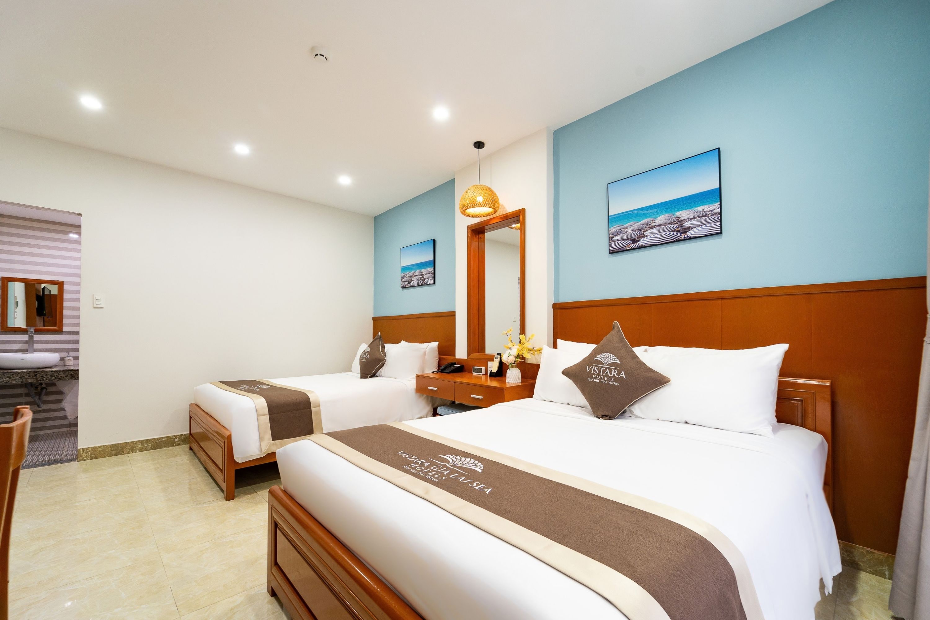 Quarto de hotel com duas camas, banheiro e vista para o mar.