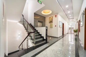 Um hall de hotel moderno com escadaria de vidro, balcão de recepção e piso estampado.