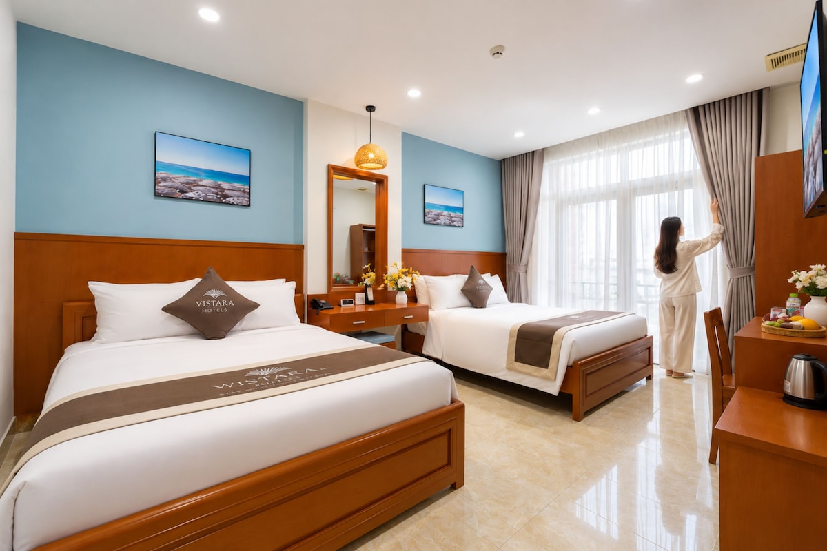 Quarto de hotel com duas camas, uma secretária com chaleira, espelho e obras de arte nas paredes.