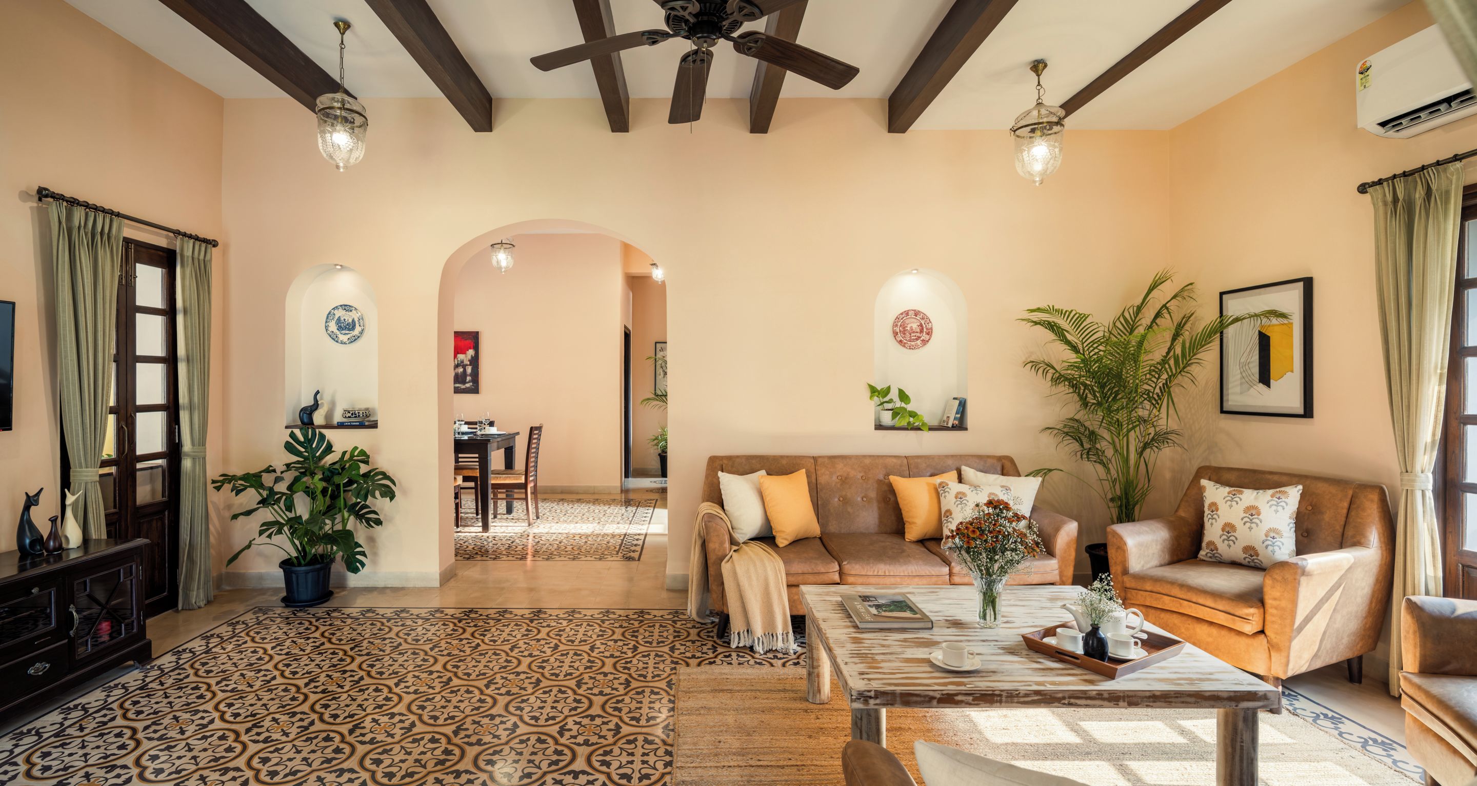 Uma sala de estar ampla, com teto alto, ventilador de teto, um sofá grande, mesa de centro e um espaço de refeições ao fundo.