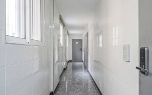 Corredor claro e bem iluminado, com paredes de azulejos brancos e chão de granito, que leva a uma porta com o número 208.
