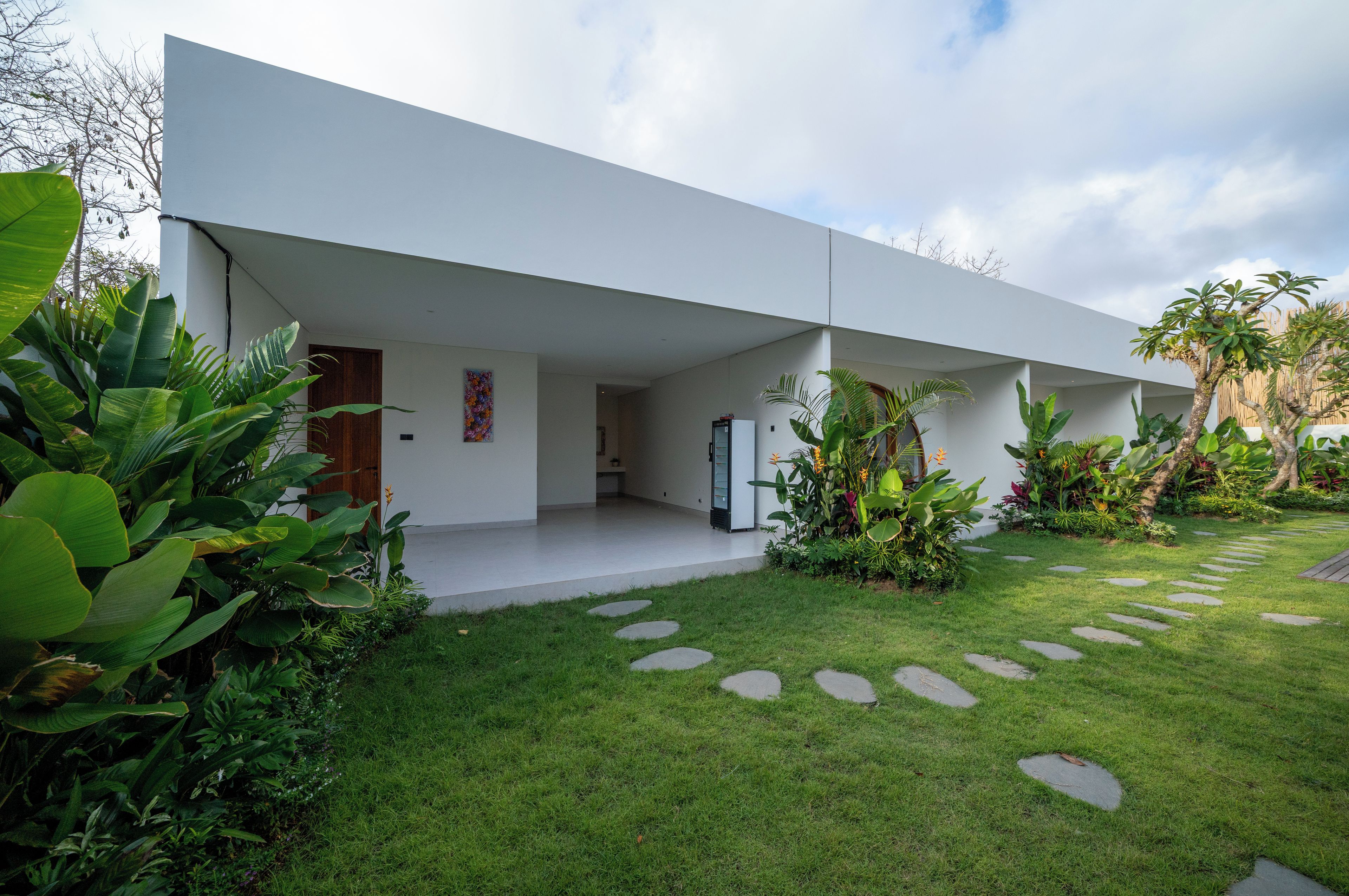 Uma casa moderna com telhado plano, varanda coberta e jardim bem cuidado com pedras no caminho.