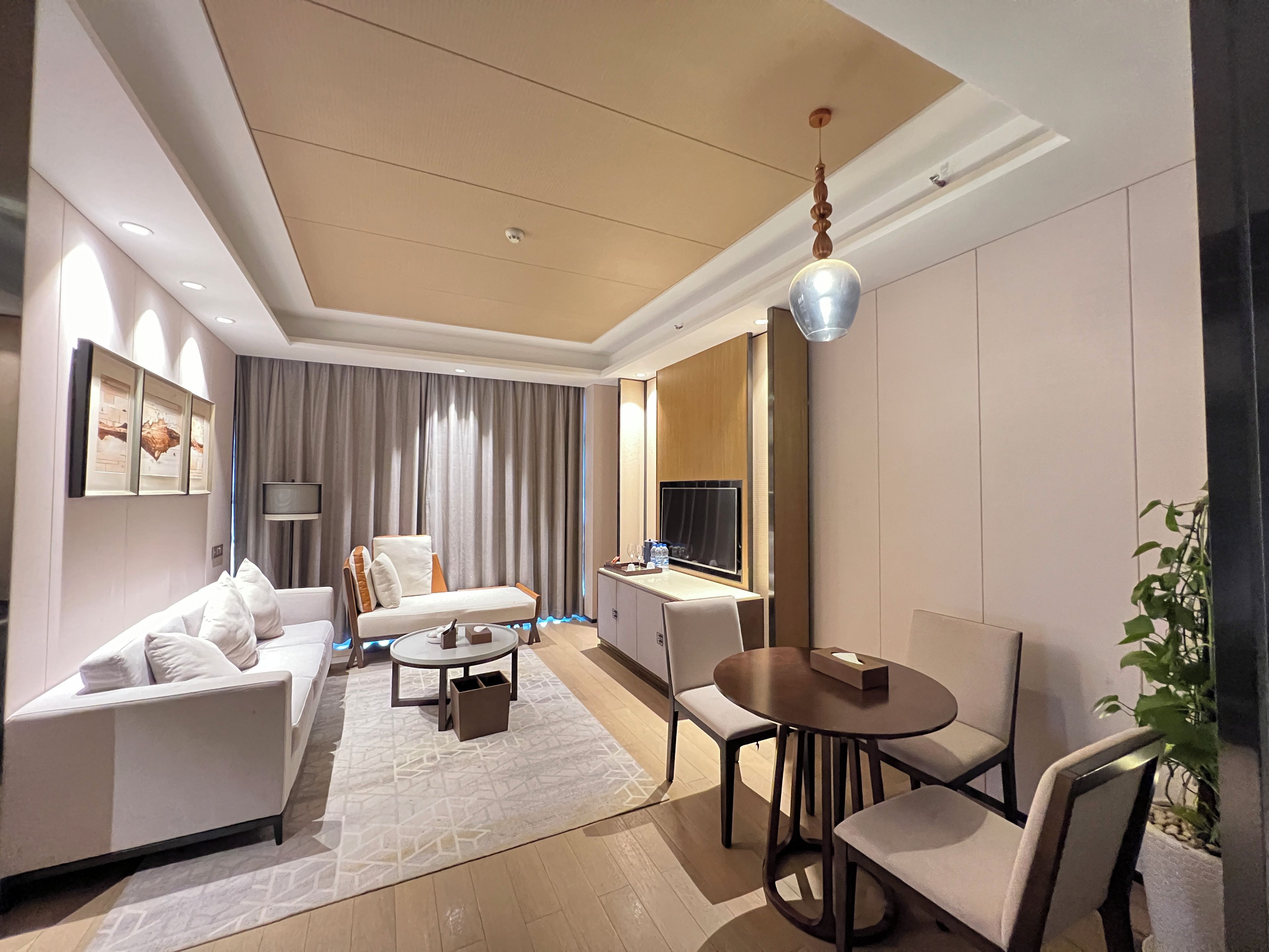Quarto de hotel moderno com sofá, mesa de jantar, TV e um espelho grande.