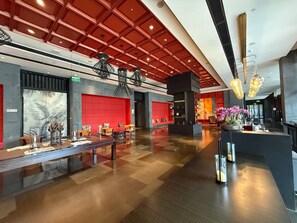 Um hall de hotel moderno com esquema de cores vermelho e preto, um balcão de recepção e uma área de estar com mesas e cadeiras.