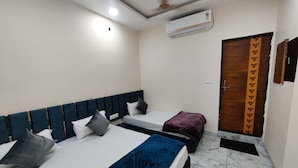 Quarto com duas camas, ventilador de teto, ar condicionado e porta de madeira com cortina estampada.