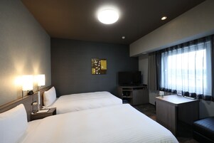 Quarto de hotel com duas camas, uma escrivaninha, televisão e janela com cortinas.