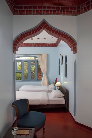 Quarto com cama, poltrona, mesa, janela e um arco decorativo.
