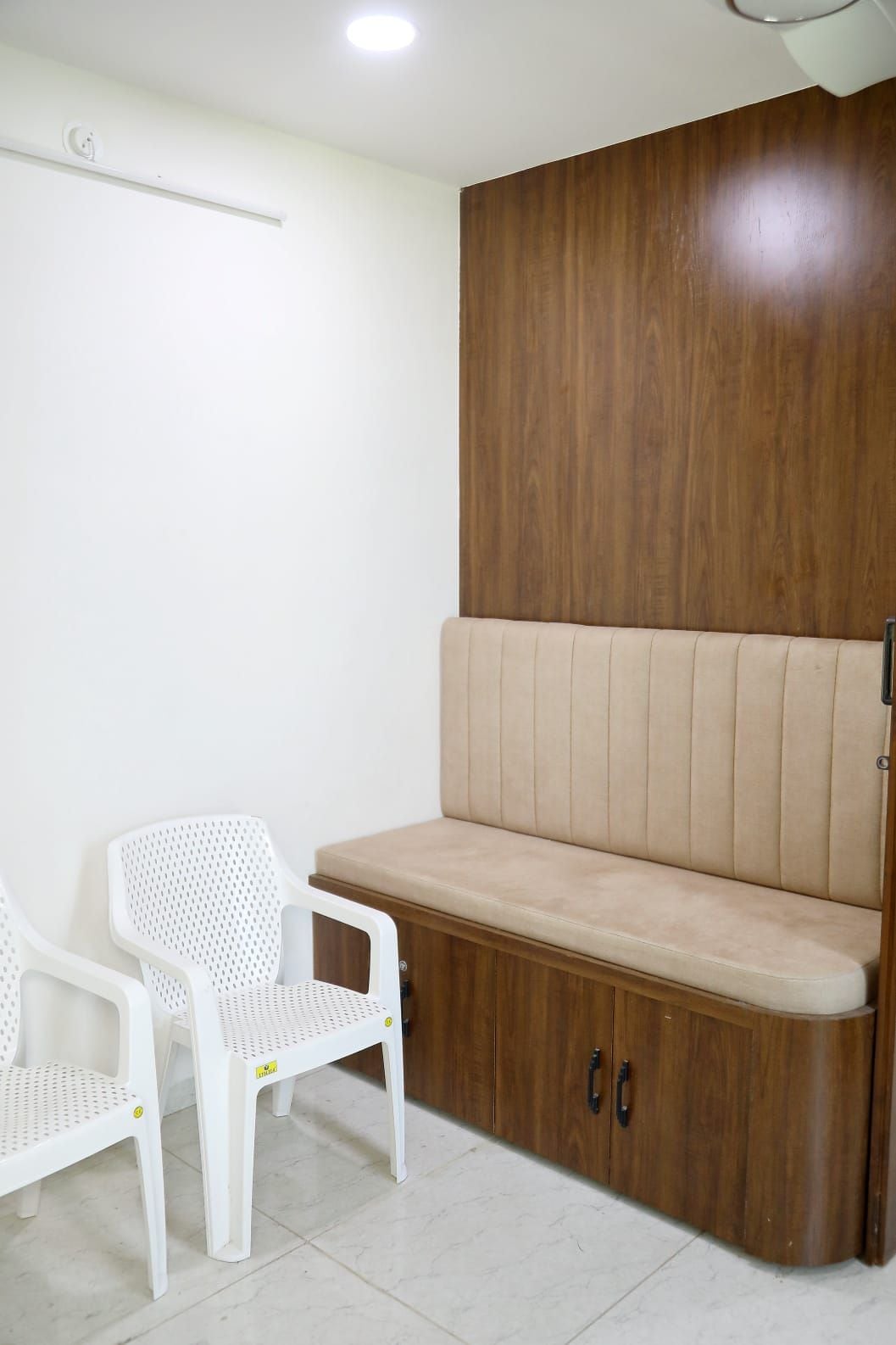 Quarto com armário de madeira, um banco e duas cadeiras brancas.