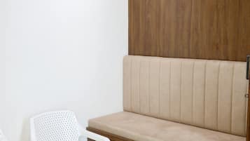 Quarto com armário de madeira, um banco e duas cadeiras brancas.