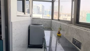 Quarto com uma janela grande, uma pequena geladeira e uma planta amarela no parapeito.