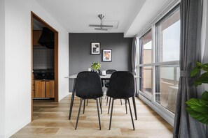 Cozinha moderna com armários de madeira, sala de jantar com cadeiras pretas e uma janela grande com cortinas.