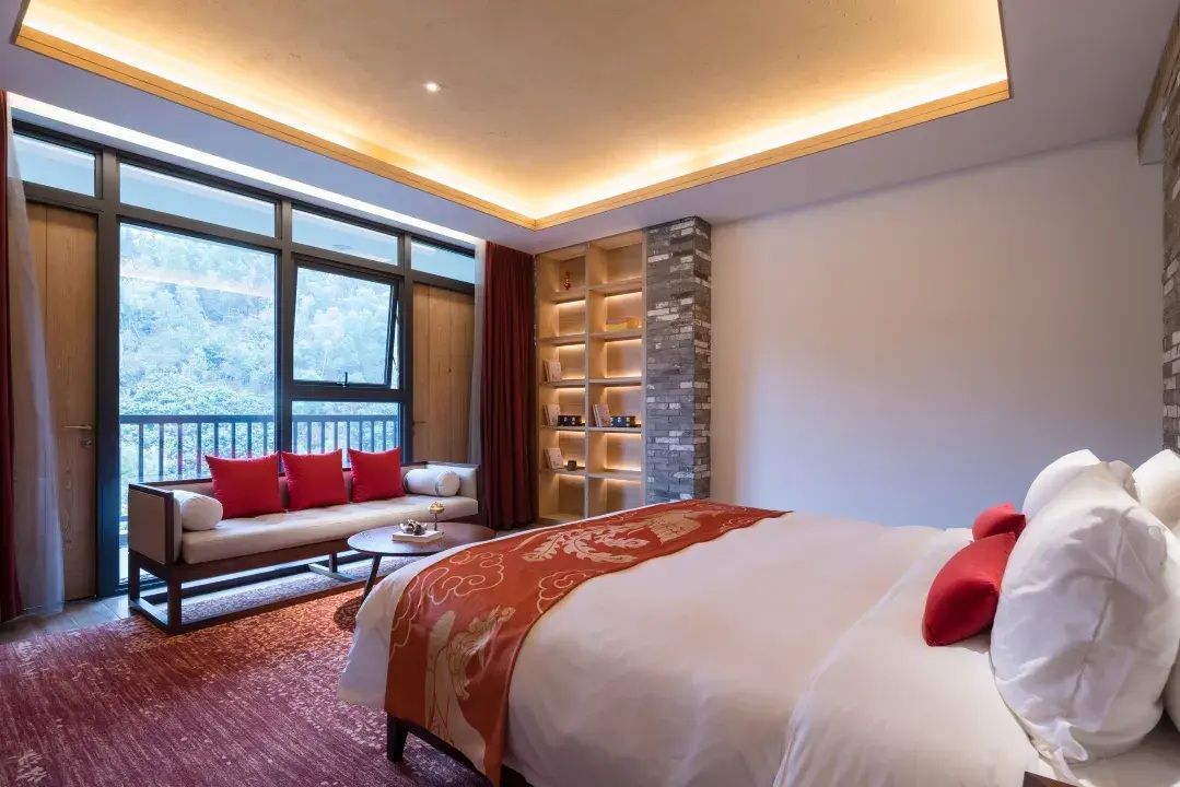 Quarto de hotel com uma cama grande, um sofá, uma mesa de centro e uma estante embutida.