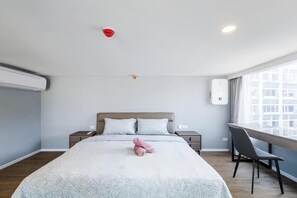 Quarto de hotel com cama, escrivaninha, cadeira, janela e ar condicionado fixado na parede.