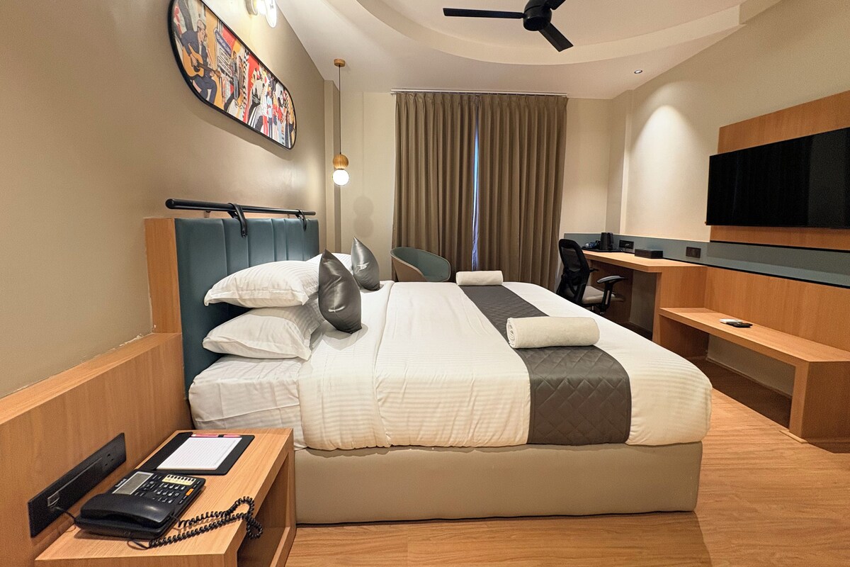 Quarto de hotel com cama, escrivaninha, cadeira e televisão de tela plana.