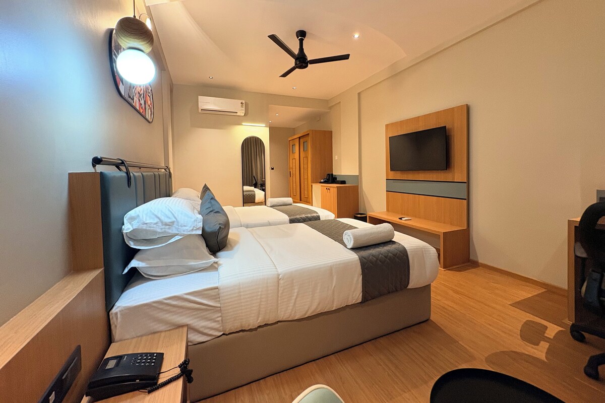 Quarto de hotel com cama, mesa de cabeceira, abajur, televisão e ventoinha no teto.