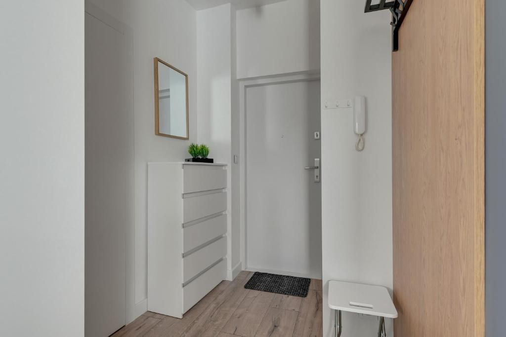 Um corredor com parede branca, uma porta, uma pequena mesa branca e uma planta sobre um armário.