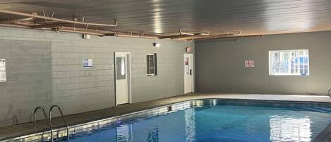 Piscina interna com piso ladrilhado, escada de metal e porta que dá para outro cômodo.