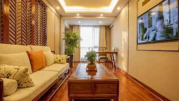 Quarto de hotel com sofá, mesa de centro, televisão e planta.