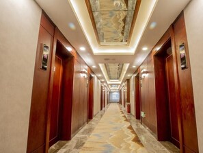 Corredor de hotel com portas de madeira, piso estampado e teto com iluminação embutida.