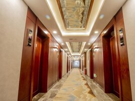 Corredor de hotel com portas de madeira, piso estampado e teto com iluminação embutida.