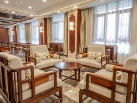 Um saguão de hotel com várias áreas de estar, incluindo sofás e poltronas, dispostas ao redor de uma mesa de centro.