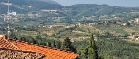 Um edifício com telhado de telhas vermelhas, varanda e vista para uma paisagem montanhosa.
