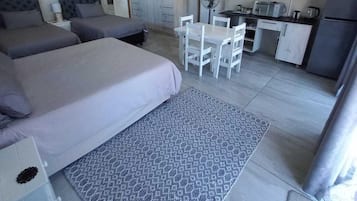 Quarto de hotel com duas camas, uma escrivaninha, televisão e cozinha compacta.
