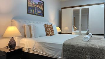 Quarto de hotel com cama, abajures, um espelho grande e um quadro na parede.