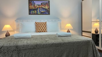 Quarto de hotel com cama, duas luminárias de cabeceira, um quadro na parede e um guarda-roupa.