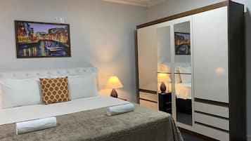 Quarto de hotel com uma cama, mesa de cabeceira, luminária, guarda-roupa e um quadro na parede.
