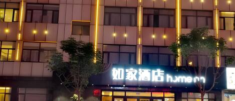 Hotel com fachada moderna, letreiros iluminados e área de estacionamento com carros.
