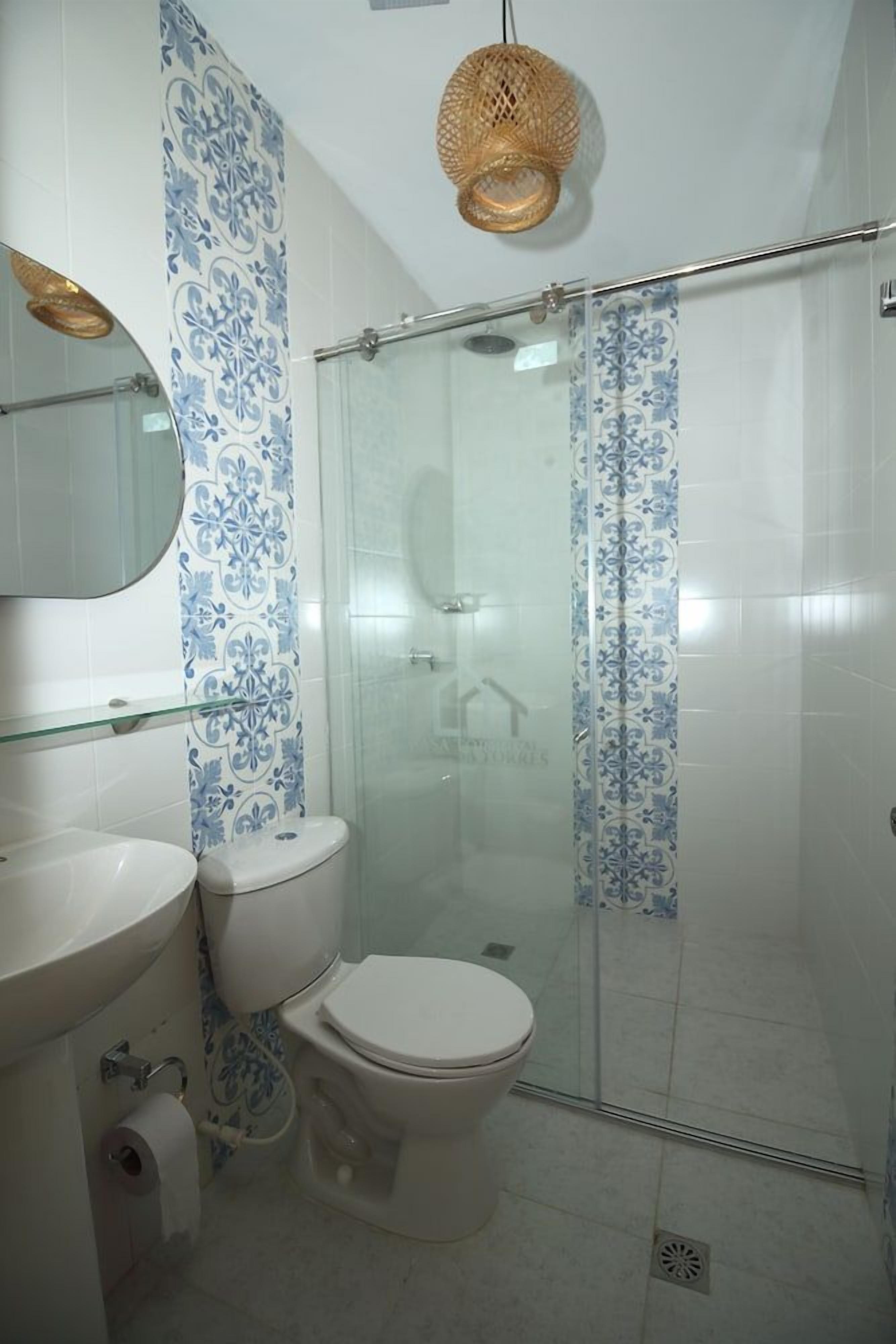 Um banheiro com box de vidro, vaso sanitário, pia e espelho.