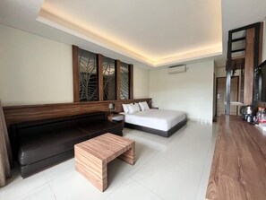 Quarto de hotel moderno com sofá, cama, mesa de centro de madeira e televisão.