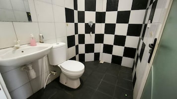 Casa de banho com uma pia branca, sanita e parede riscada a preto e branco.
