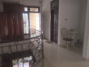Interior residencial com varanda, porta de madeira, mesa pequena com cadeira e piso de azulejos.