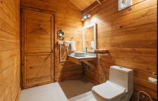 Casa de banho com painéis de madeira, incluindo sanita, lavatório, espelho, porta-toalhas e porta.