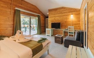 Quarto de cabana de madeira com cama, escrivaninha, televisão e varanda com área de estar ao ar livre.