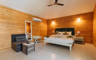 Quarto com painéis de madeira, uma cama, um espelho, uma mesinha, um sofá e um ventilador de teto.