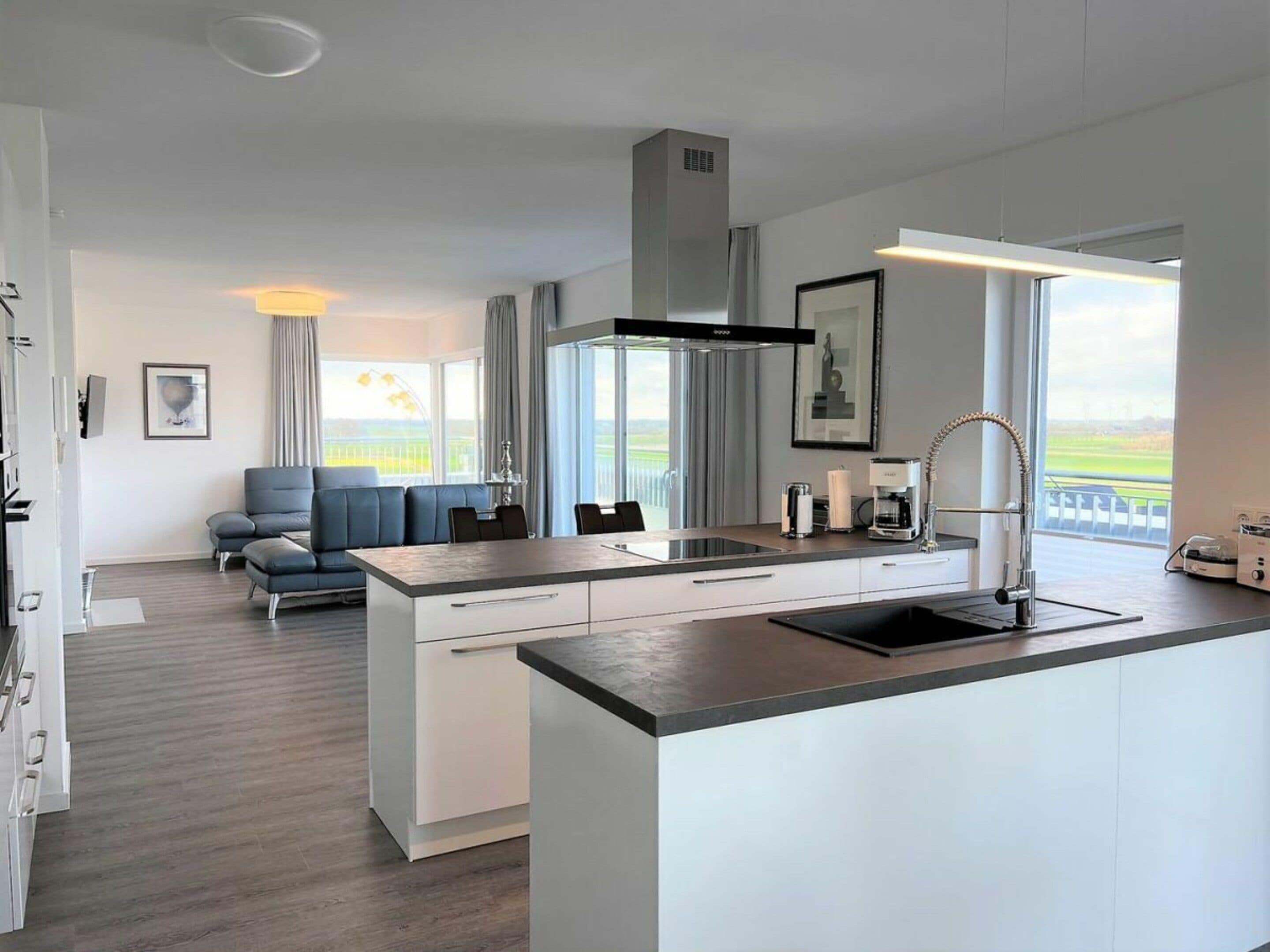Cozinha moderna com ilha central, área de jantar com sofá e grandes janelas com vista para o exterior.