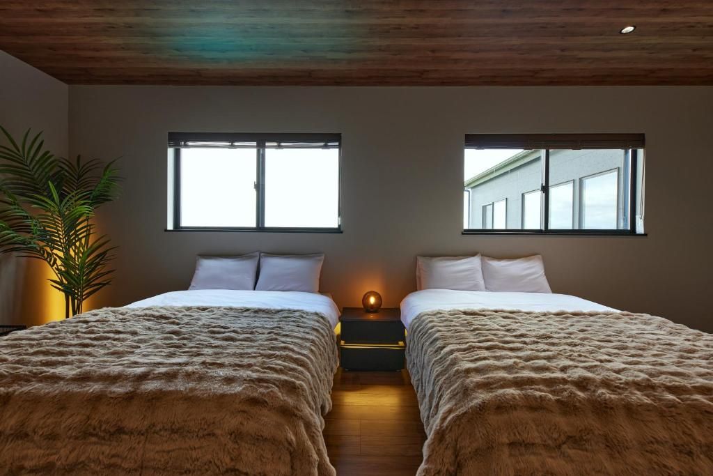 Quarto com duas camas, mesa de cabeceira, abajur e uma grande planta em vaso.