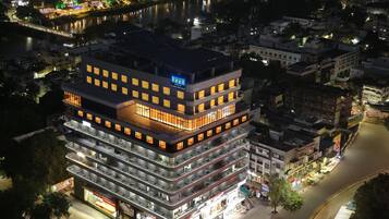 Um hotel com vários andares e design moderno, com entrada destacada, várias varandas e vista para o rio.