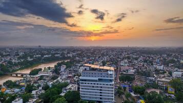 Paisagem urbana ao pôr do sol, com um rio, edifícios e um hotel alto e imponente.