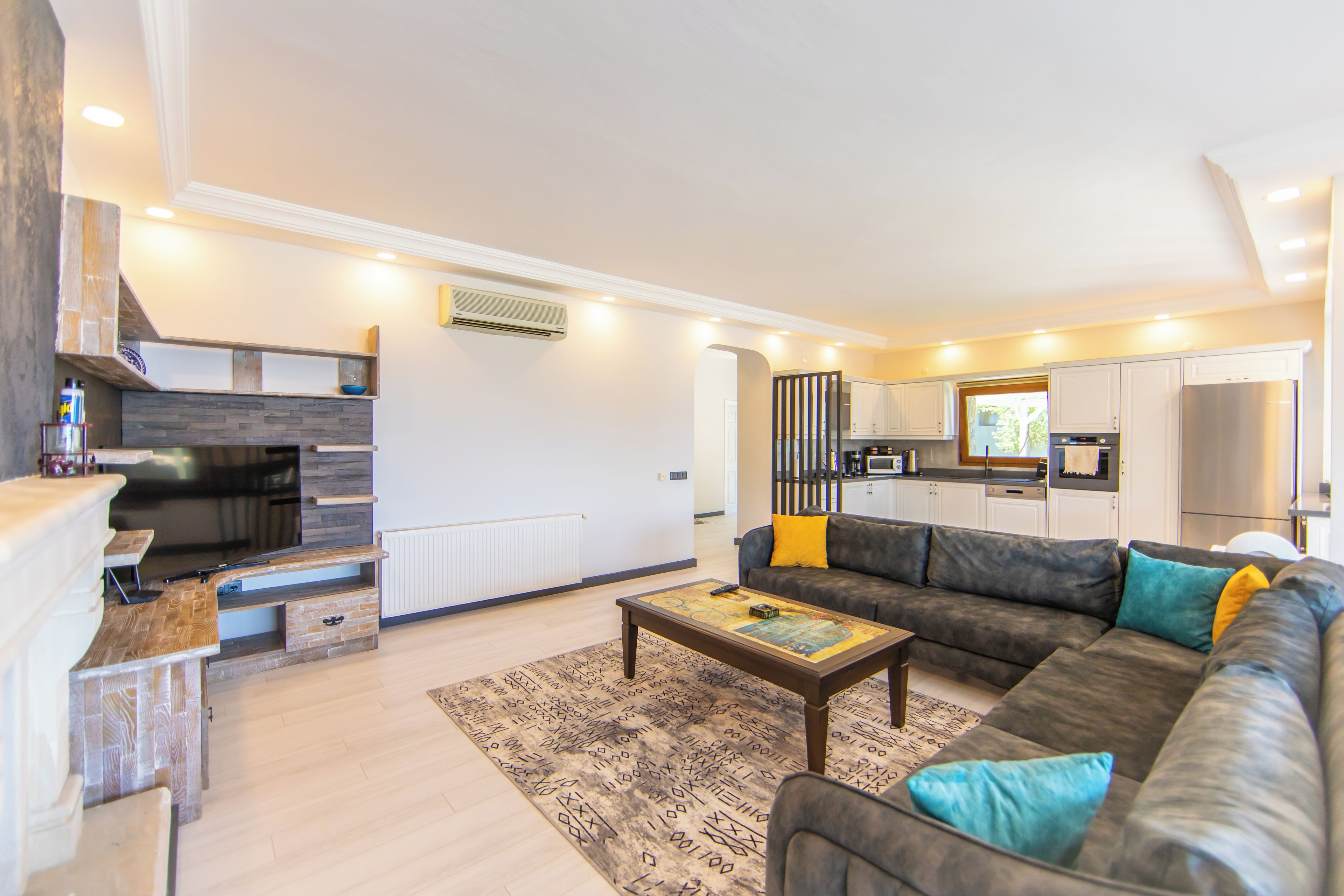 Uma sala de estar moderna com lareira, um sofá, uma mesa de centro e uma cozinha ao fundo.