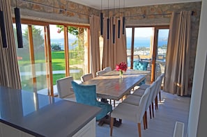 Uma sala de jantar com uma mesa grande, cadeiras e vista para o mar.