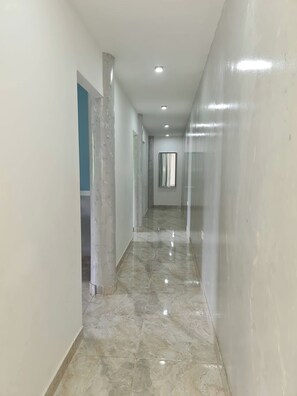 Corredor com piso brilhante, paredes brancas e luminária embutida no teto.