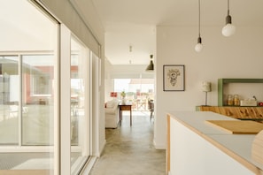 Cozinha moderna com uma ilha grande, área de jantar com mesa e cadeiras, e vista para o exterior por uma porta de vidro deslizante.